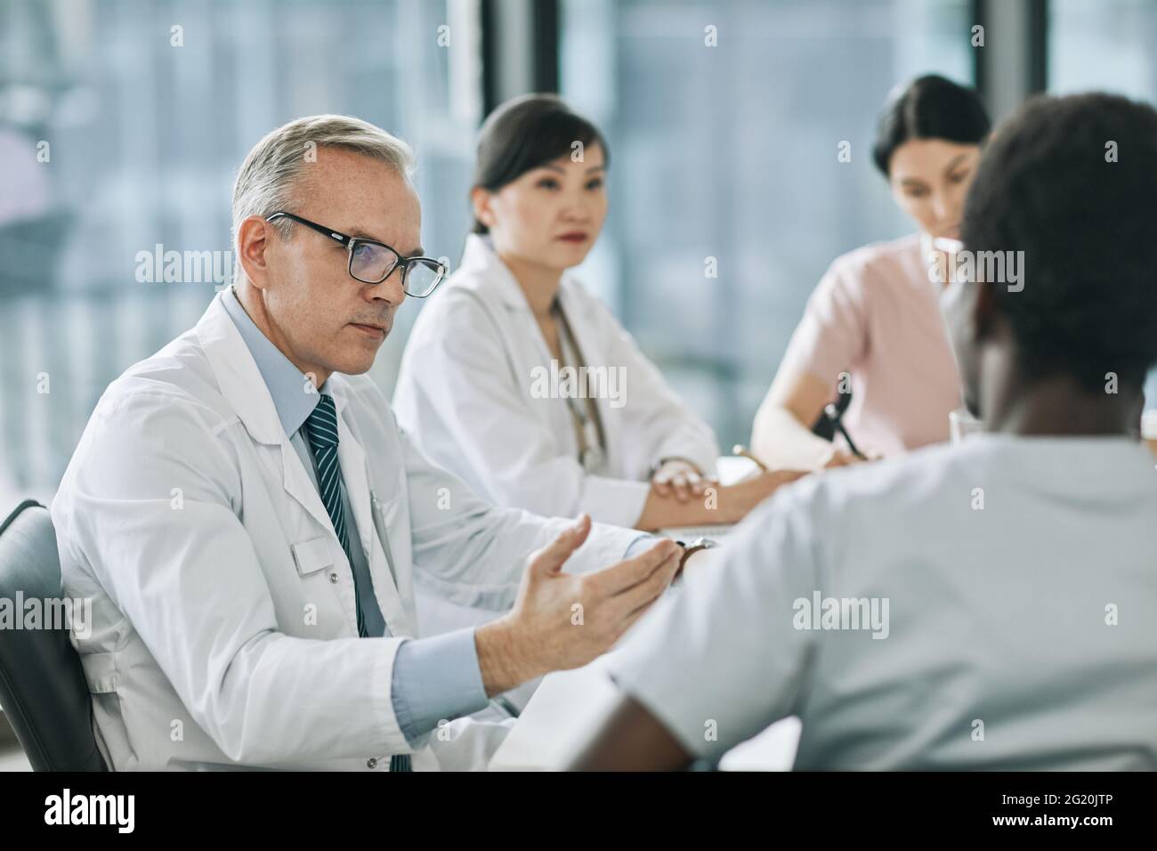 Portrait of expert doctor talking to colleagues while sitting at ...