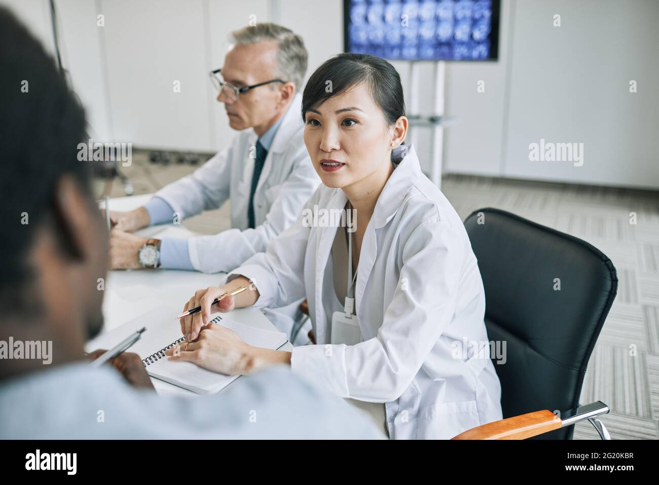 Portrait of young female doctor talking to colleagues at meeting table ...