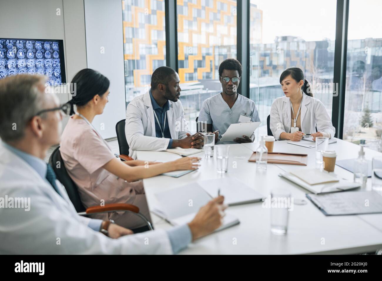 Large group of doctors discussing case while sitting at meeting table ...