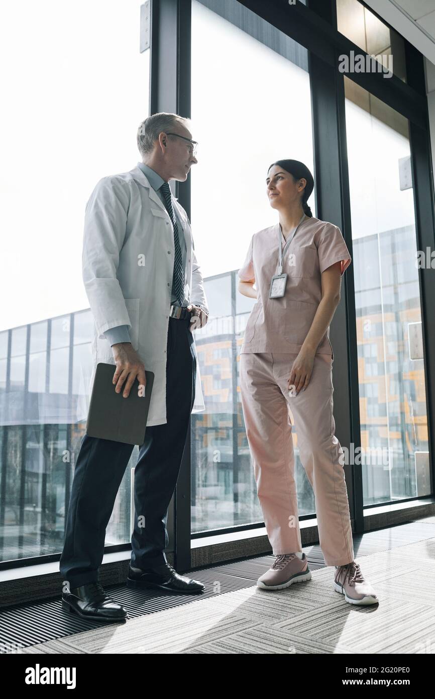 Vertical full length portrait of two doctors talking in modern clinic ...