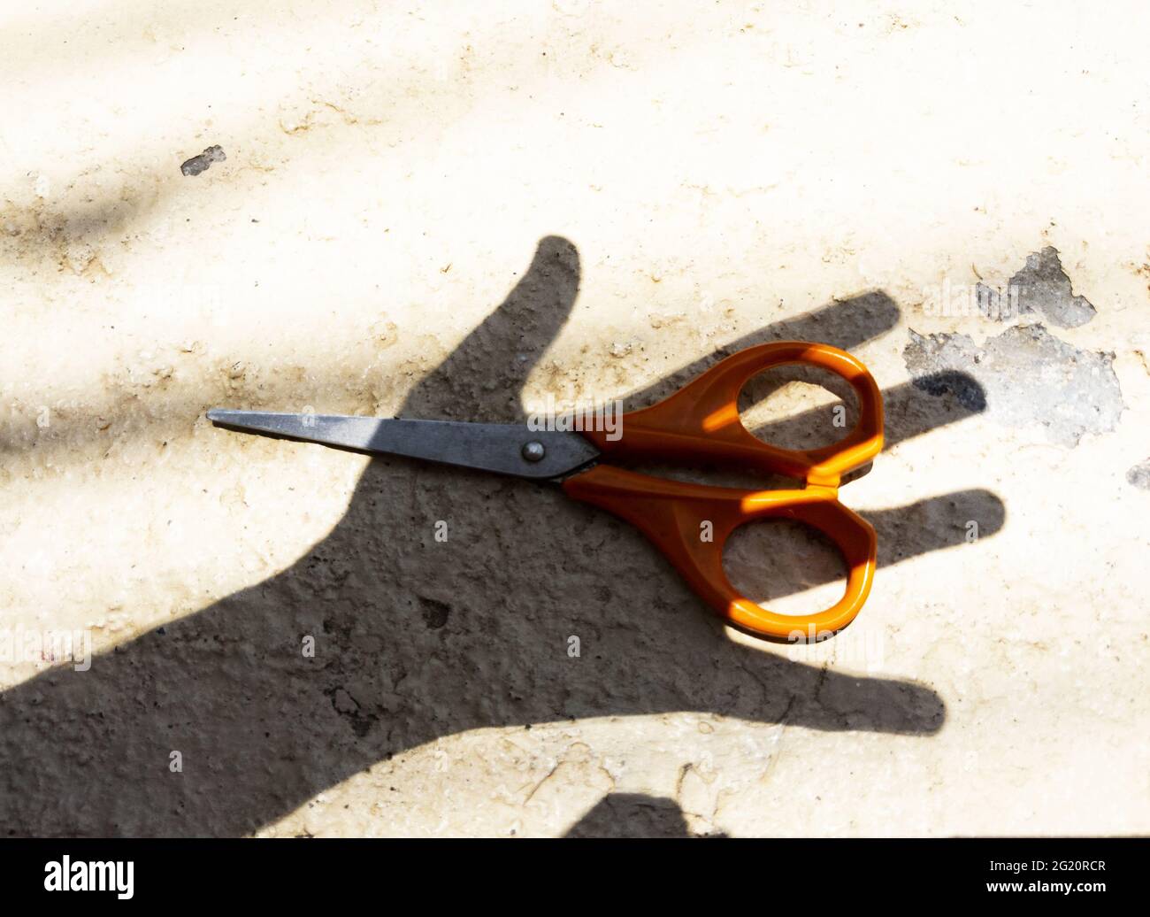 Hand shadow over a pair of orange scissors Stock Photo - Alamy