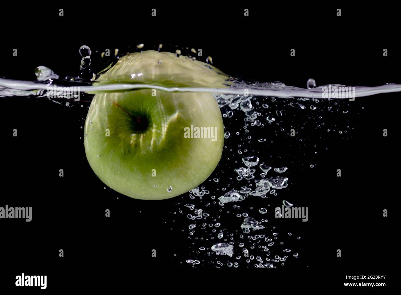Ripe green apple falling down into clear water with splashes against ...