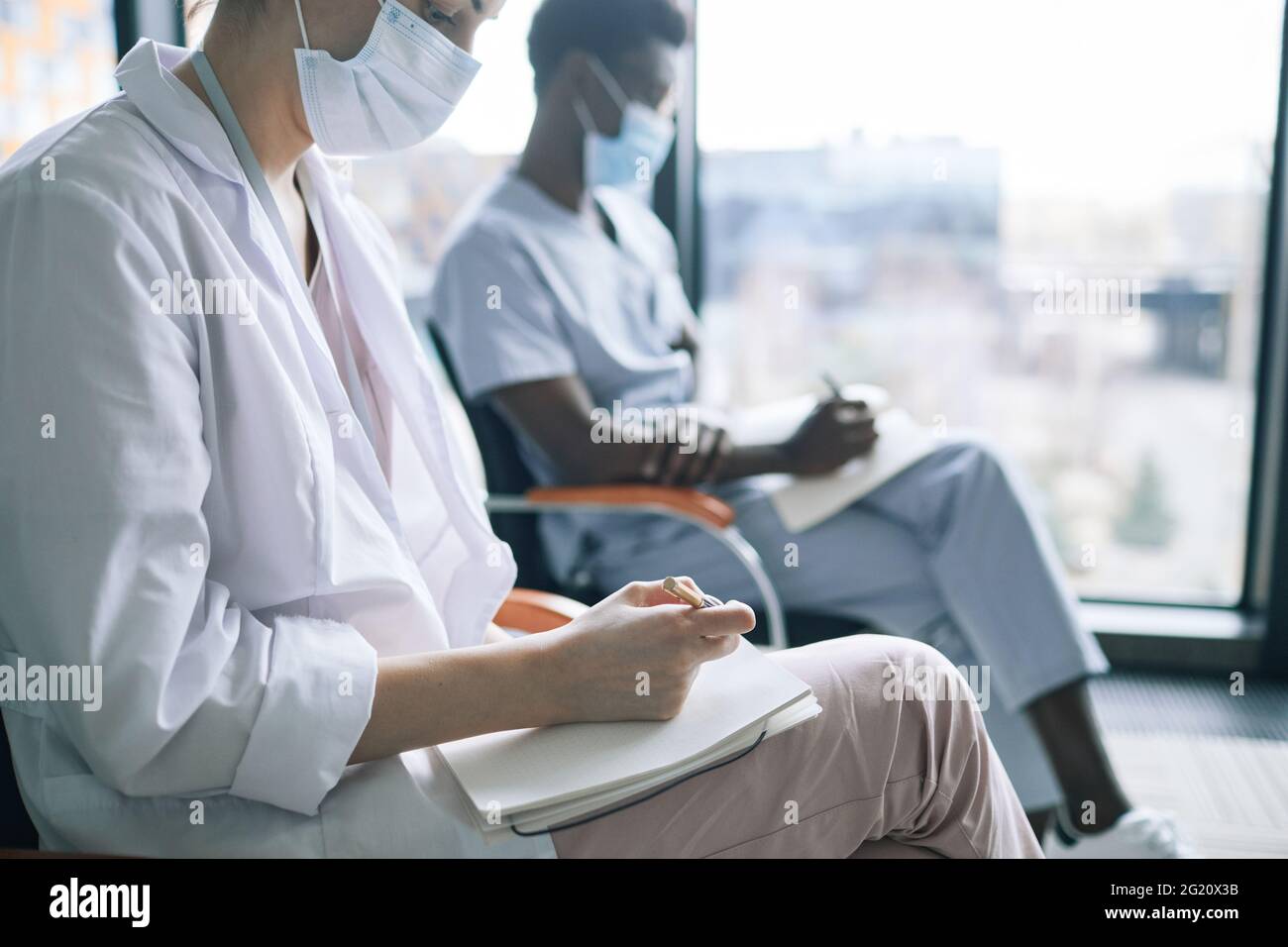 Side view at doctors taking notes while sitting on chairs during ...