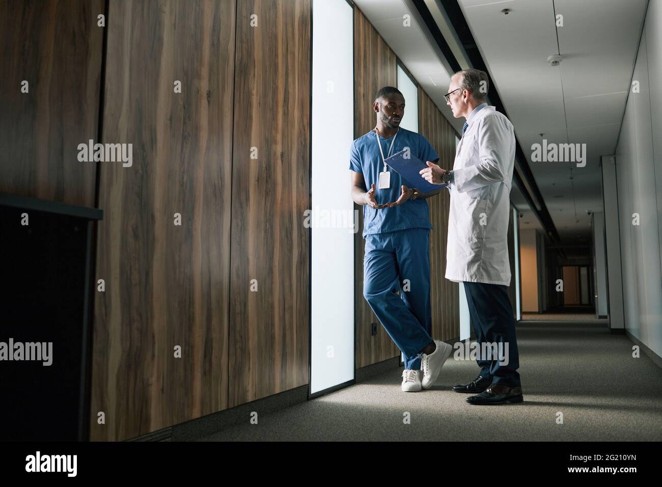 Full length portrait of two doctors talking while standing in clinic ...