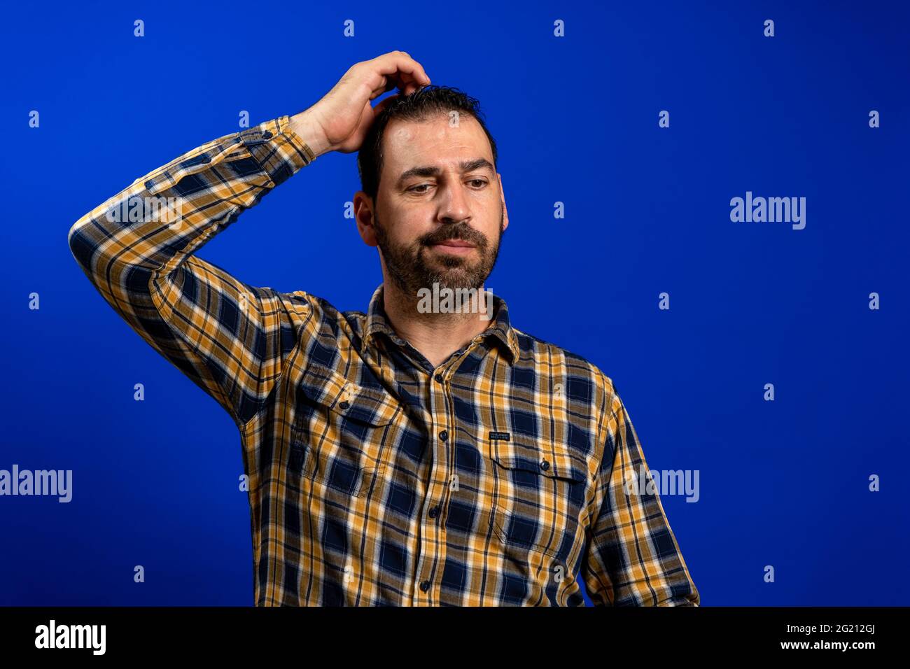 Bearded man in a yellow plaid shirt scratching his head while ...