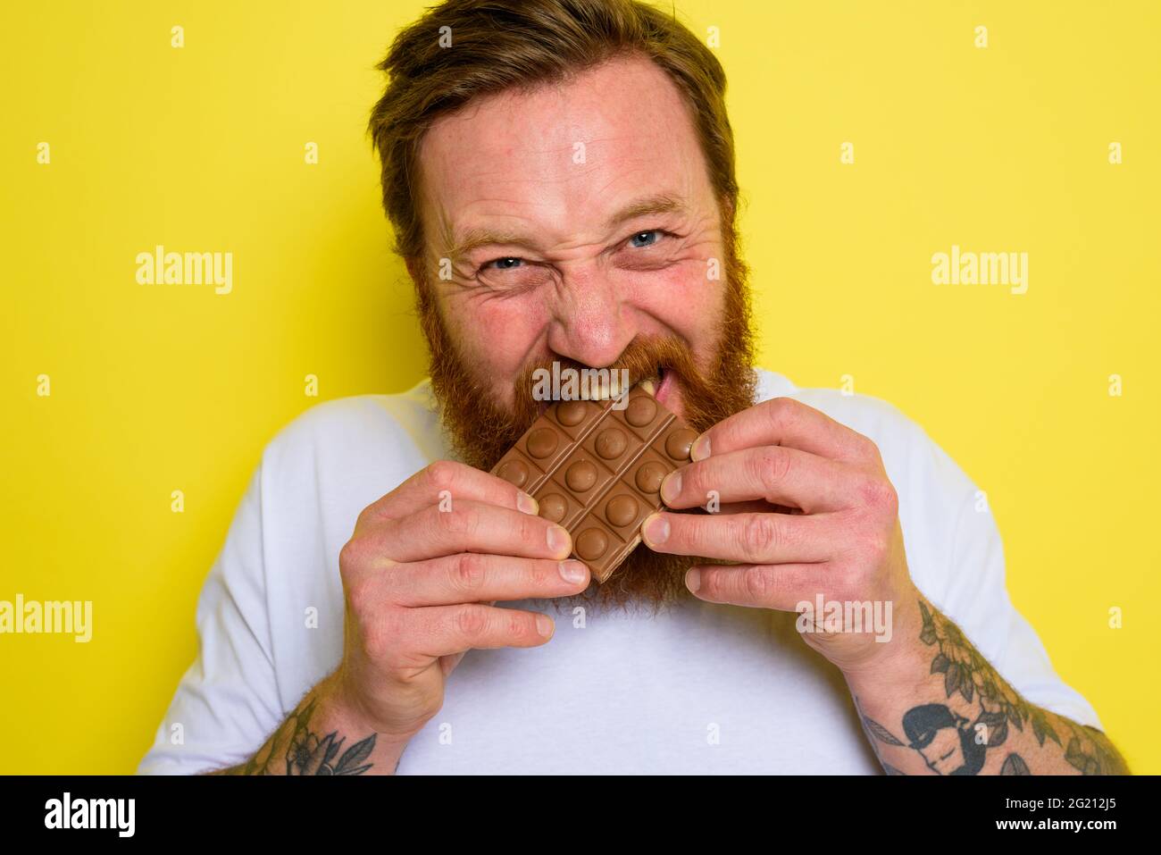 Happy man with beard and tattoos eats chocolate Stock Photo - Alamy