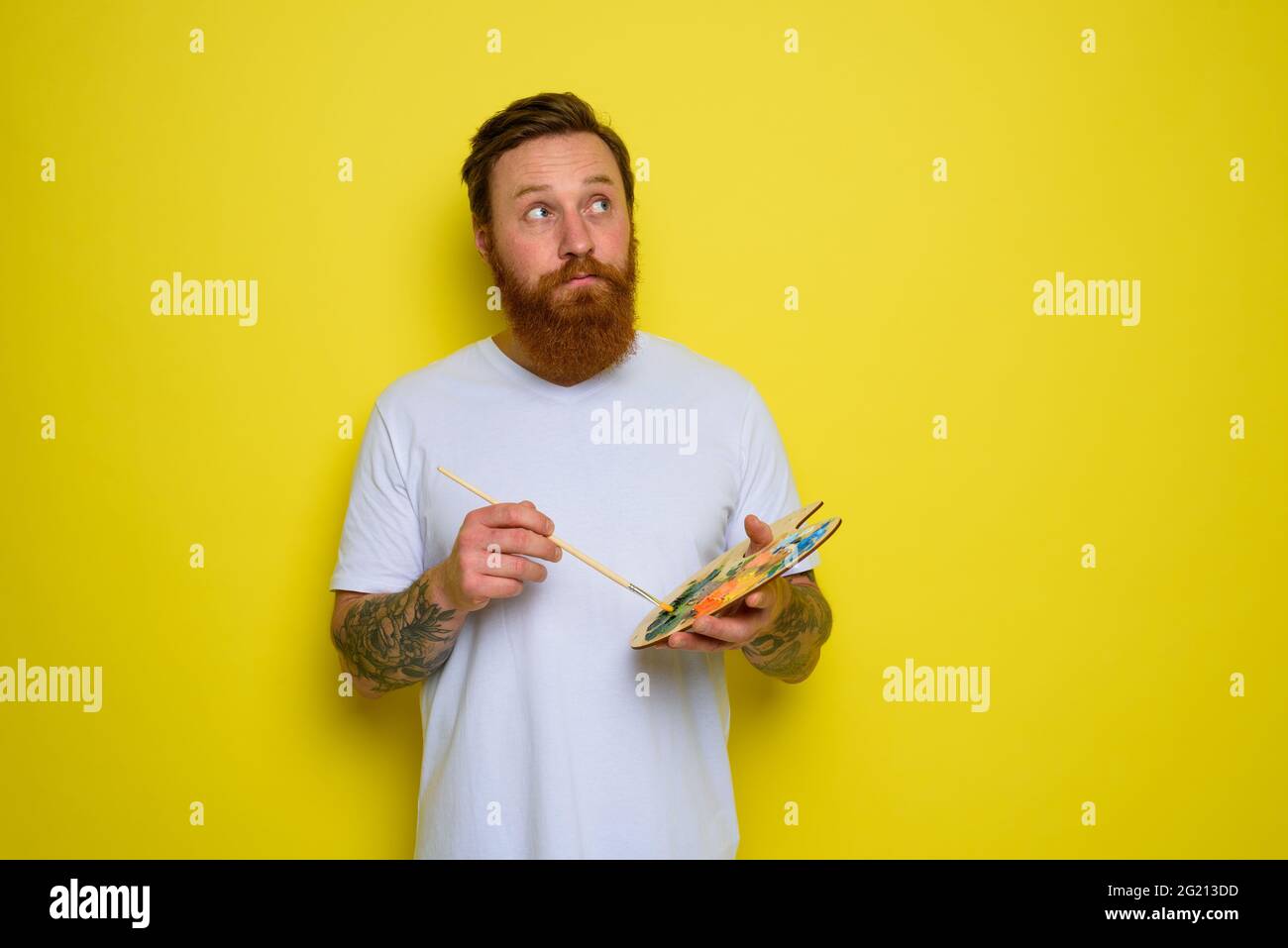 Undecided man with beard and tattoo is ready to draw with brushes Stock ...