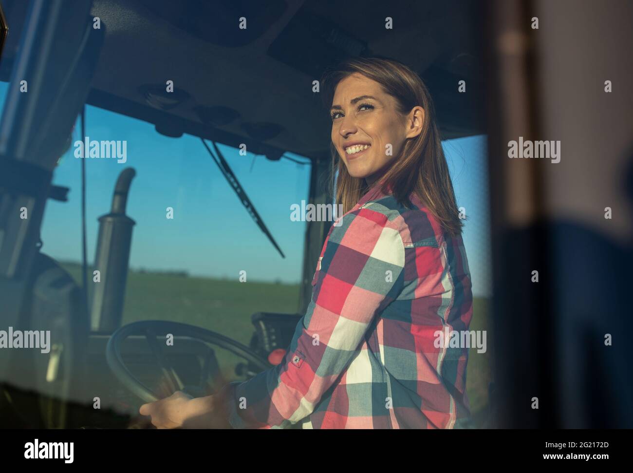 Young farmer sitting in tractor driving in field. Female agronomist ...
