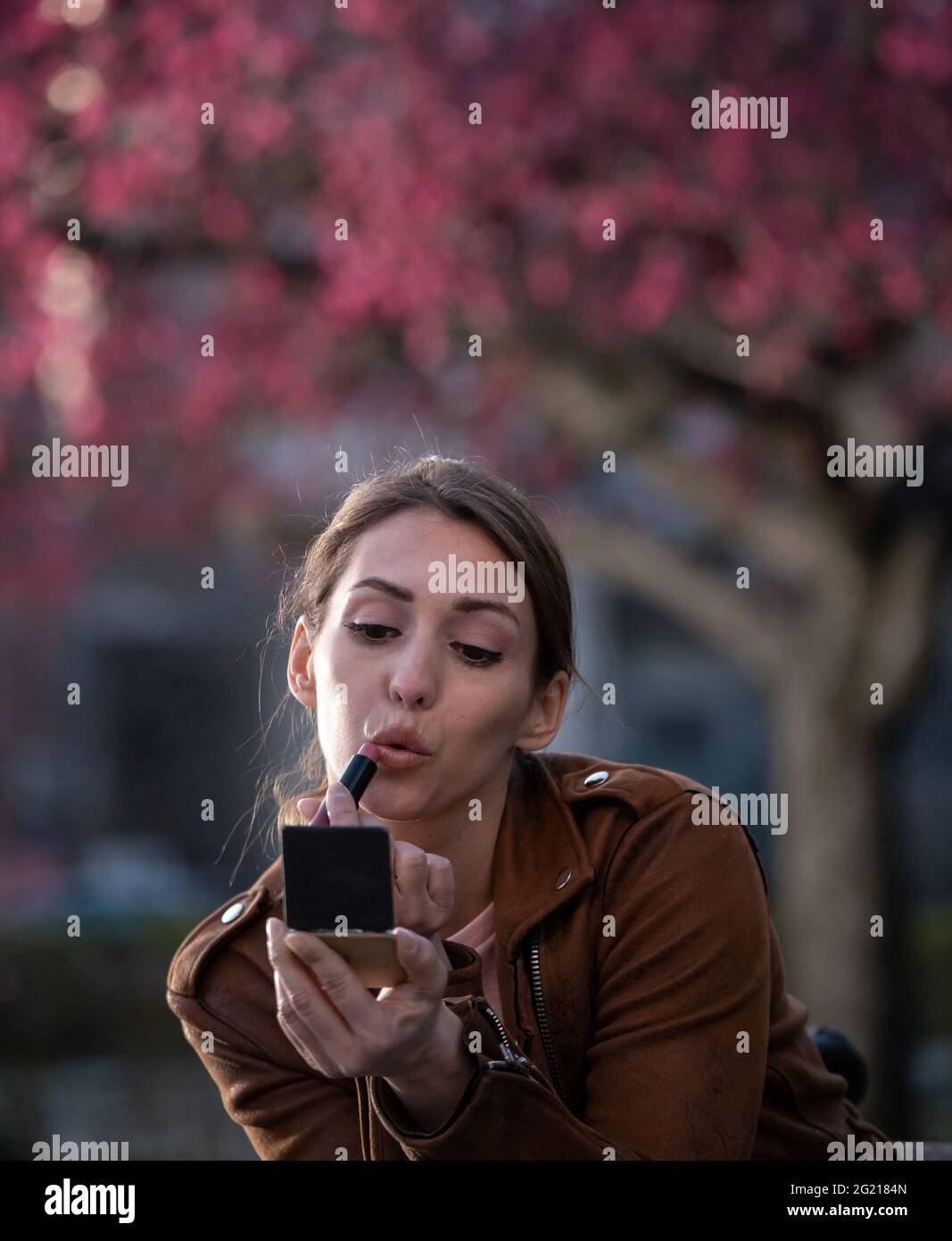 Student putting on lipstick in park. Young attractive woman using ...