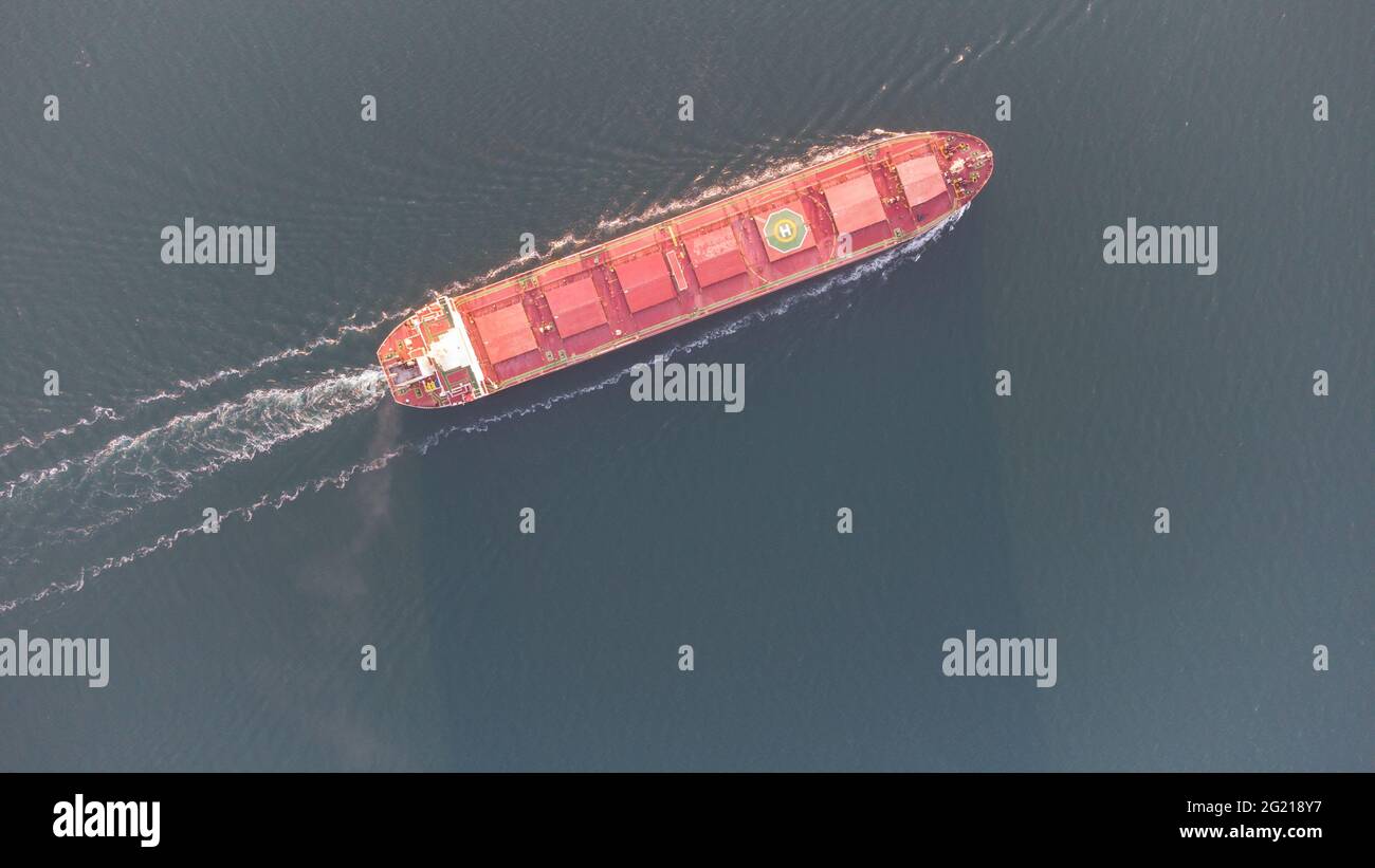 A large ocean-going cargo ship moves out to sea on calm waters. Dry ...