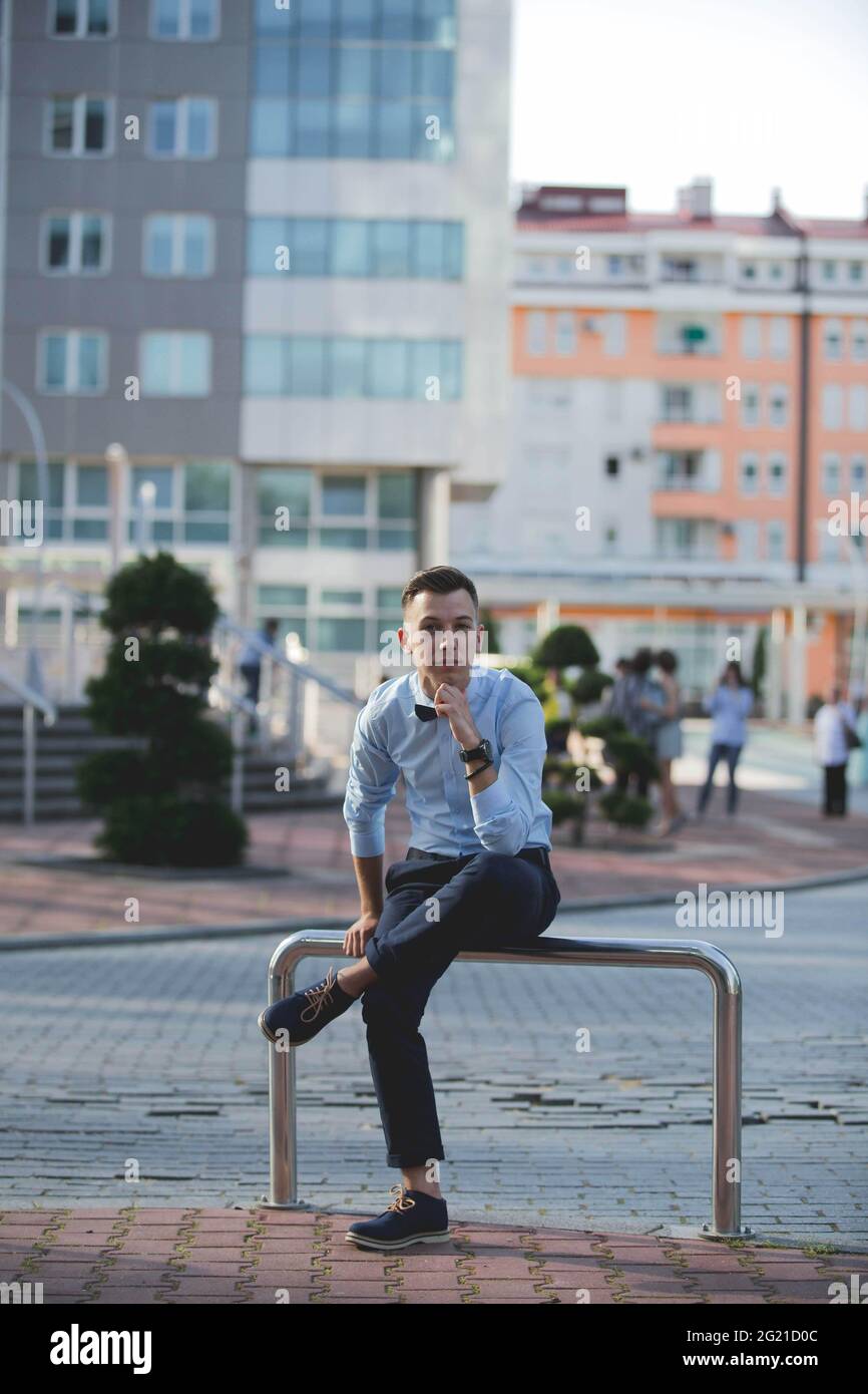 Stylish young man in a suit sitting on metal parking barrier with his ...