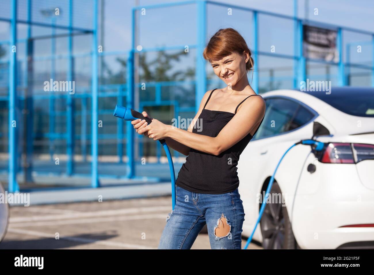 Beautiful young girl next to an electric car. Posing and holding a ...