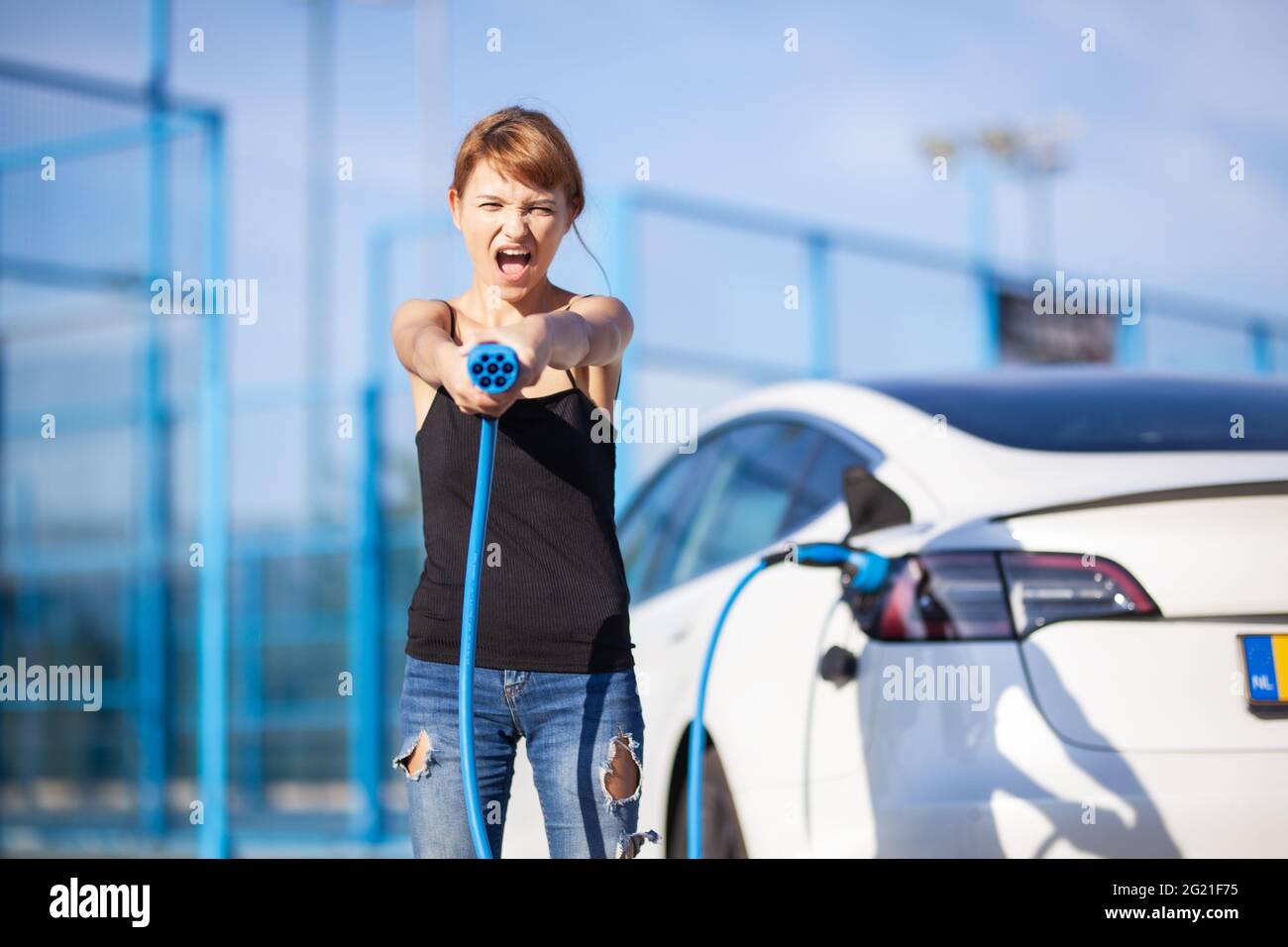 Beautiful young girl next to an electric car. Posing and holding a ...