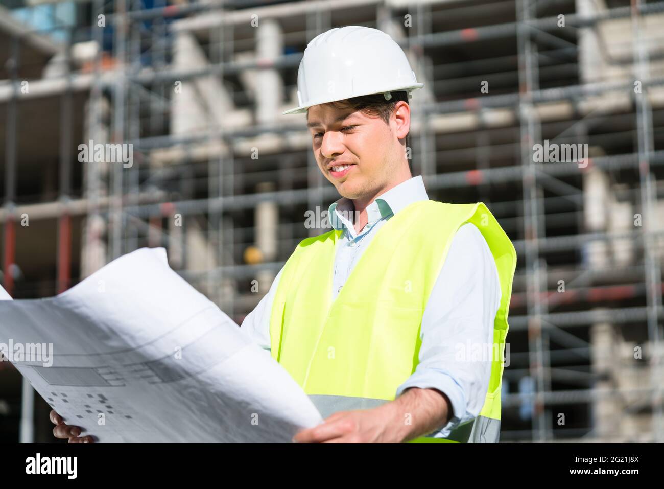 Construction engineer studying floor plan in front of building shell at ...