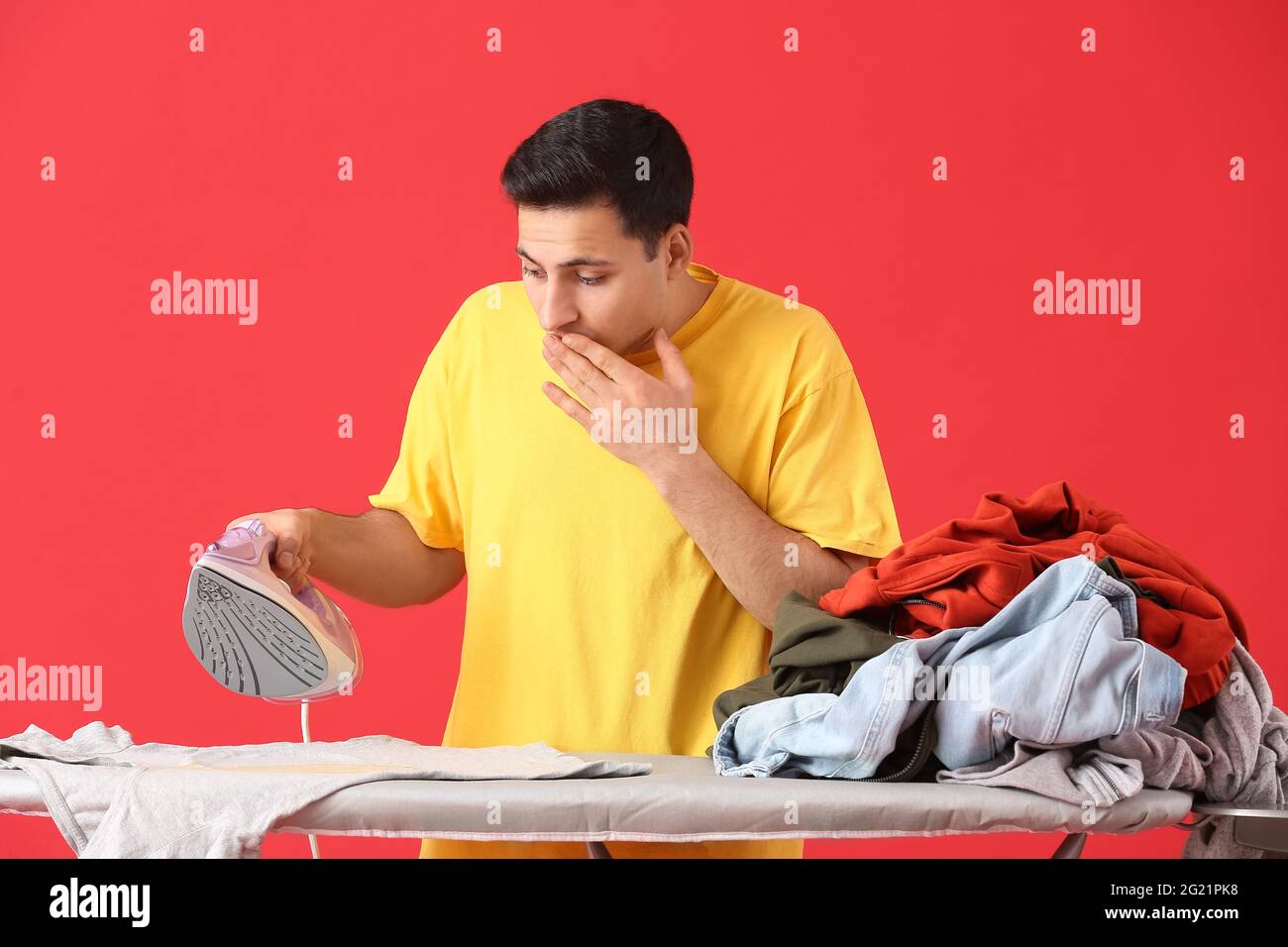 Shocked young man ironing clothes on color background Stock Photo - Alamy