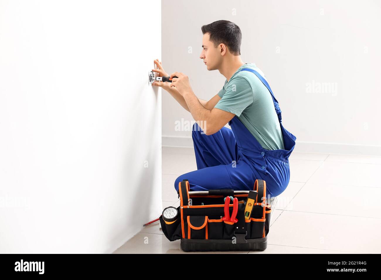 Young electrician repairing socket in room Stock Photo - Alamy