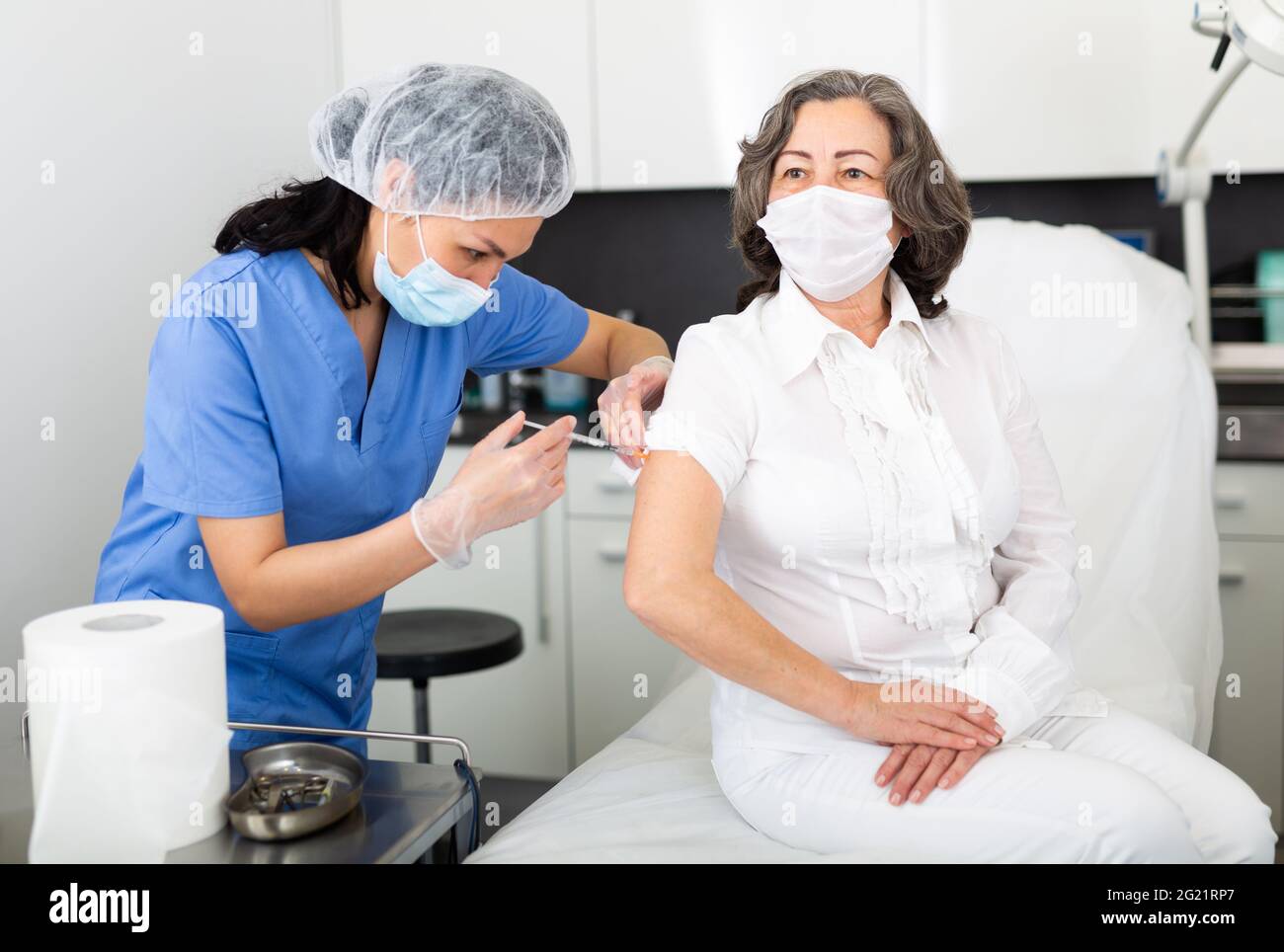 Professional female nurse injecting vaccine in shoulder of female ...
