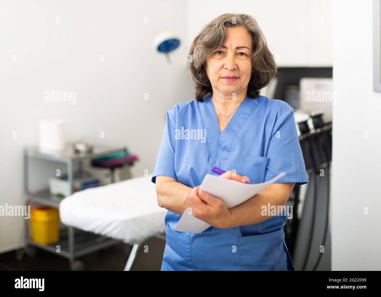 Aged woman cosmetologist standing with papers in aesthetic cosmetology ...