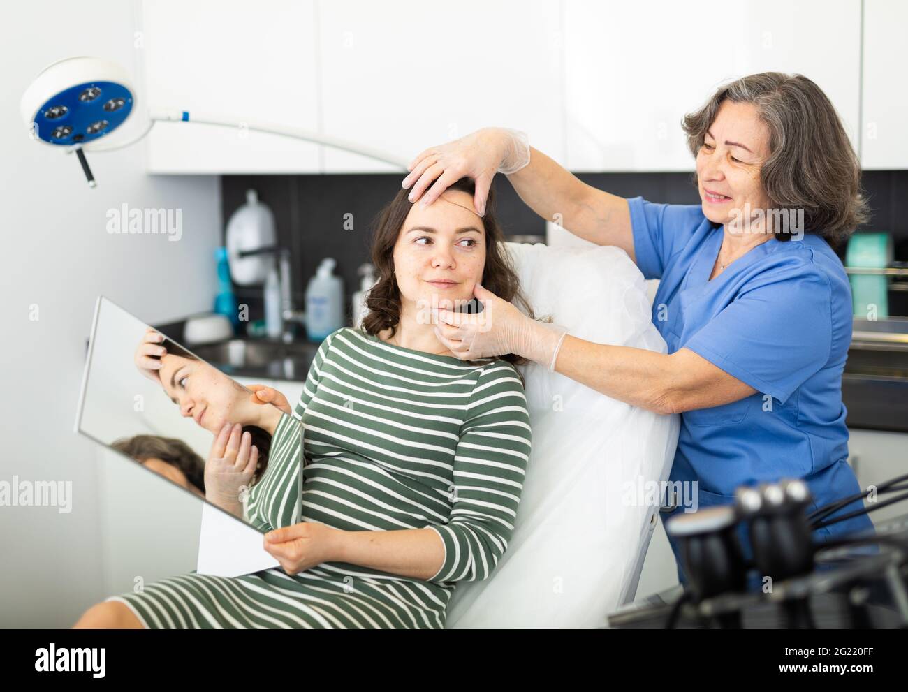 Cosmetologist examining female client face before procedure Stock Photo ...