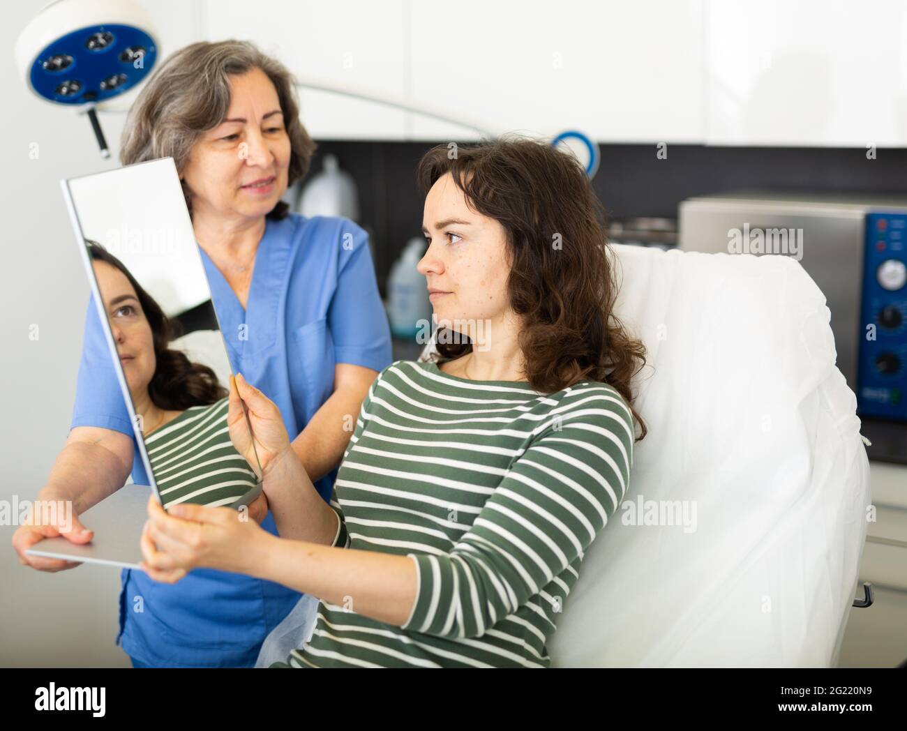 Cosmetologist examining female client face before procedure Stock Photo ...