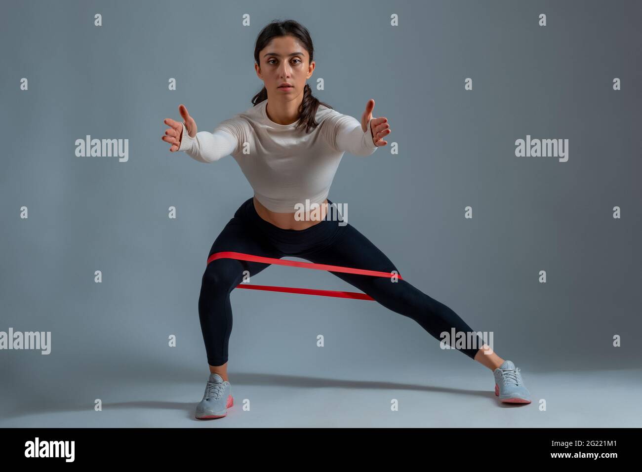 Woman performing lateral lunges with resistance band on grey background ...