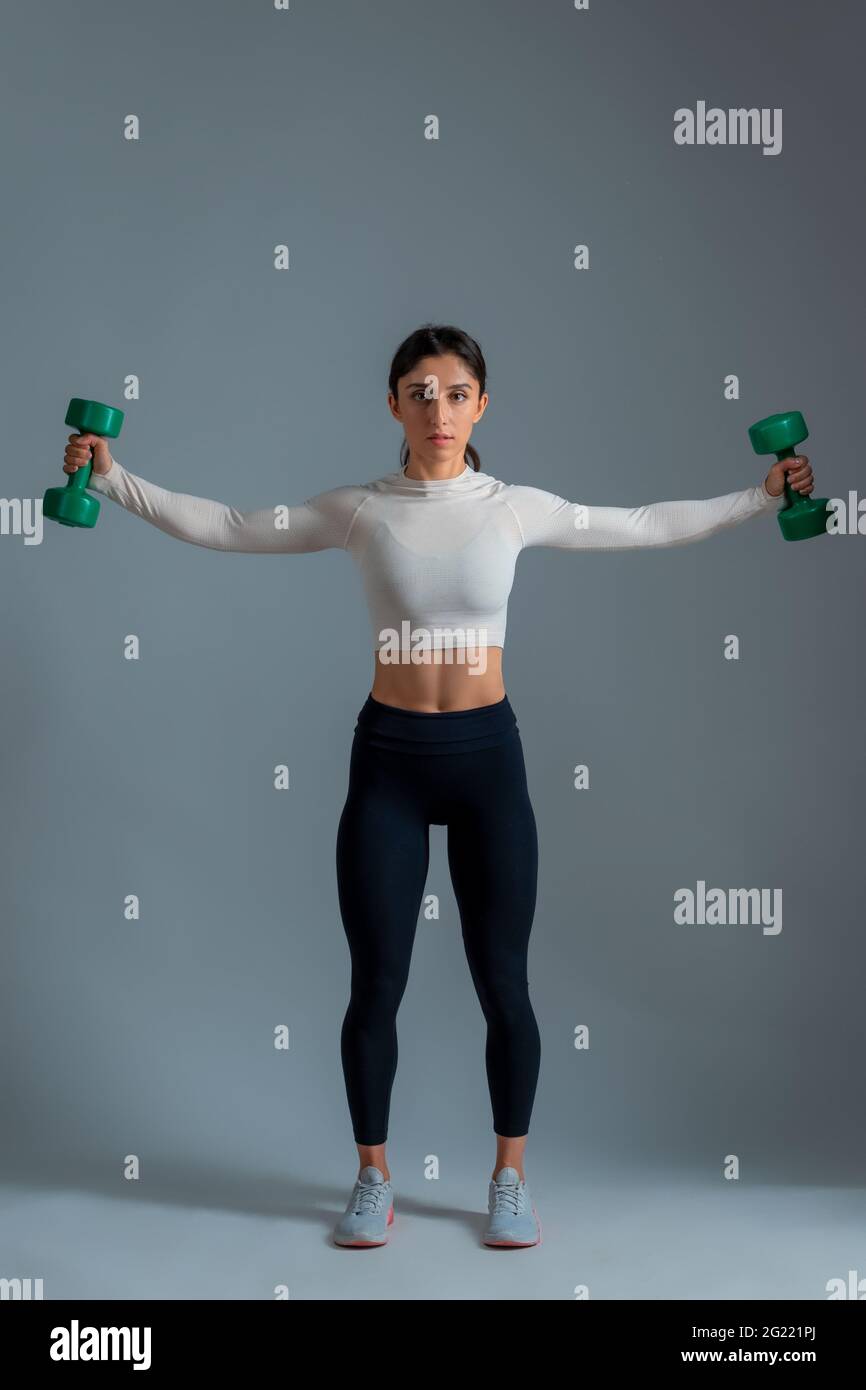 Girl performing set of shoulder exercises with dumbbells on grey ...