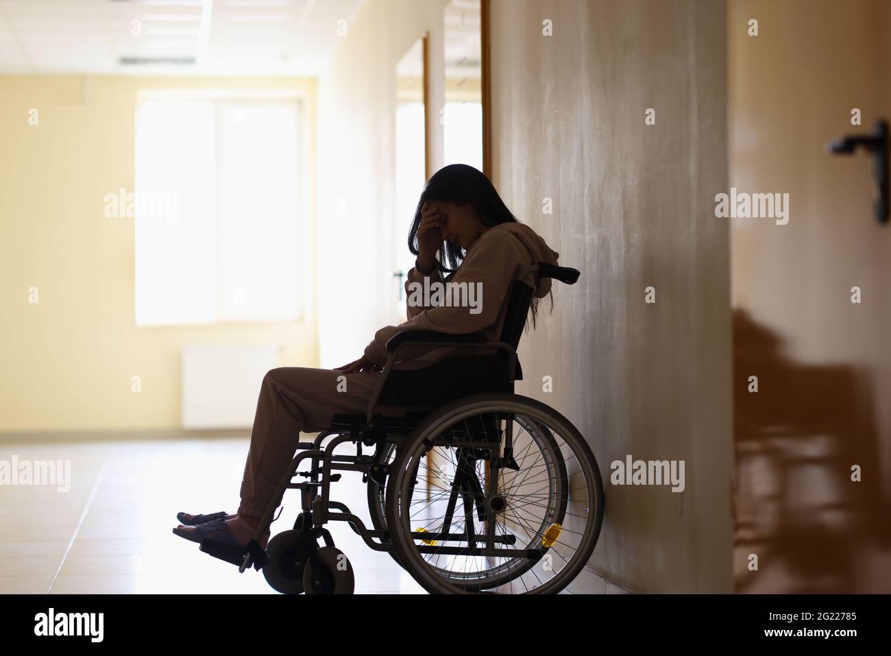 Sad woman disabled sitting in wheelchair and holding her head in clinic ...