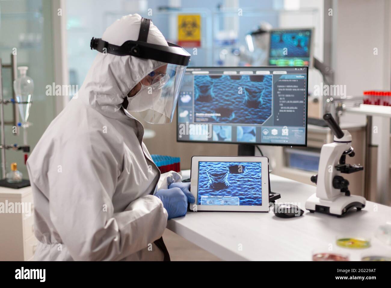 Laboratory chemist wearing ppe suit using tablet pc with virus on ...
