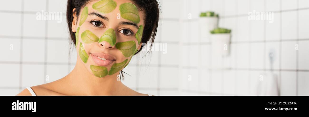 young woman with green mask on face looking at camera in bathroom ...