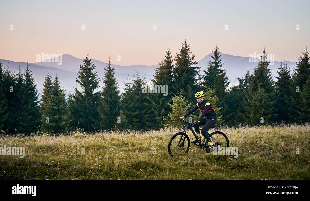 Horizontal snapshot of man cyclist riding his bicycle in the mountains in early foggy morning ...