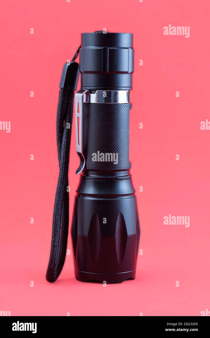 A black flashlight of powerful light standing on a red background. The ...
