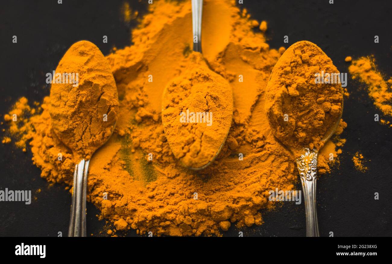 Spices turmeric in a spoon on a dark background, seasonings and herbs ...