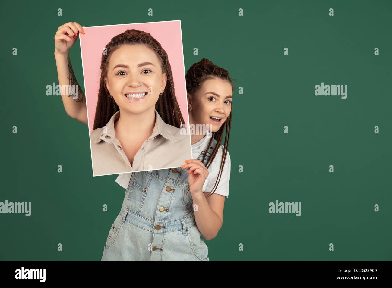 Young girl holding her portrait isolated over green studio background ...