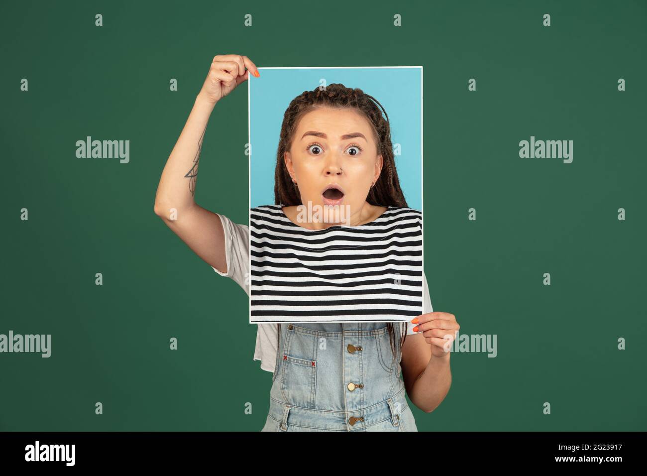 Young girl holding her portrait isolated over green studio background ...