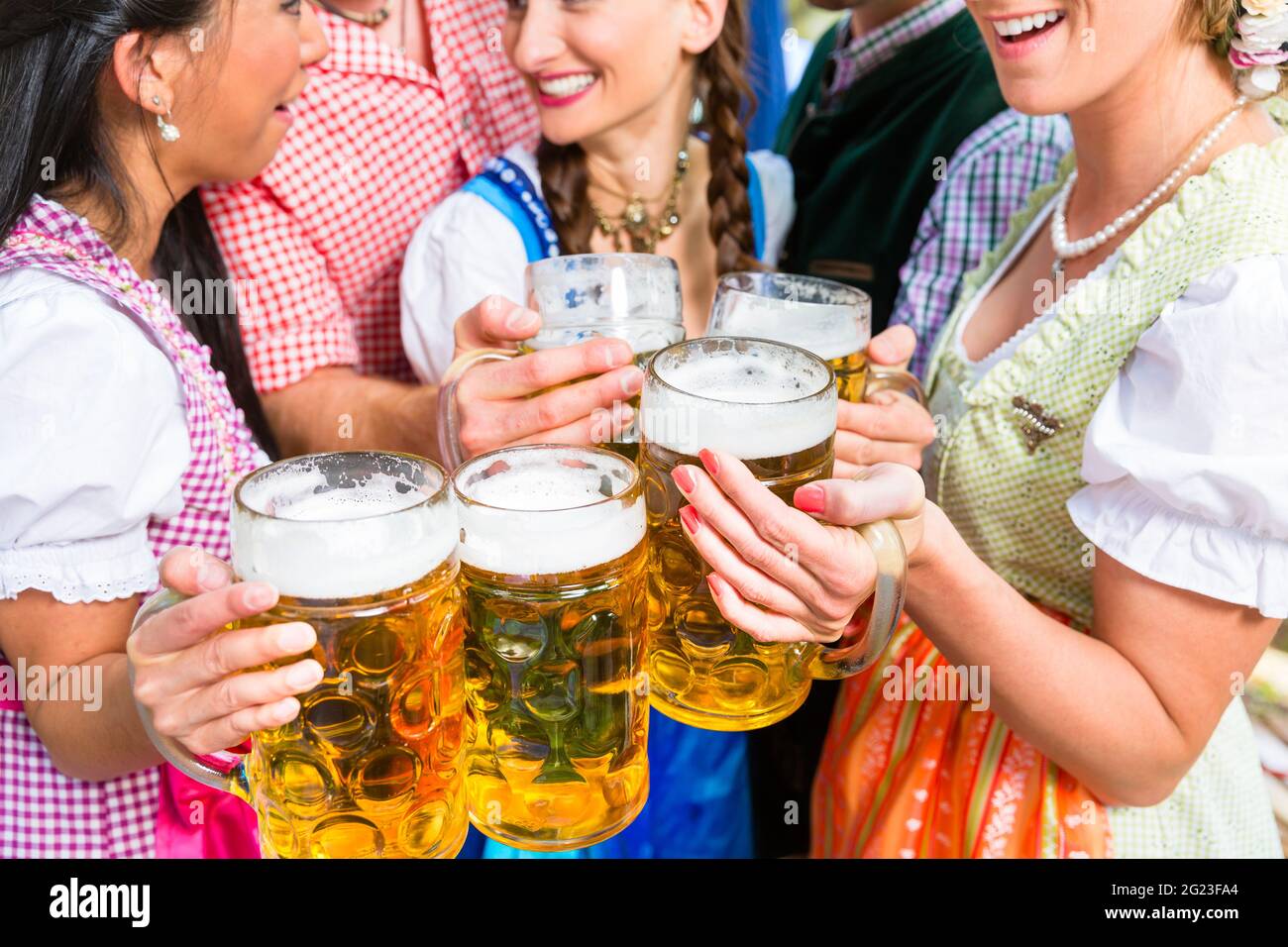 Five friends, men and women, having fun in beer garden clinking glasses ...