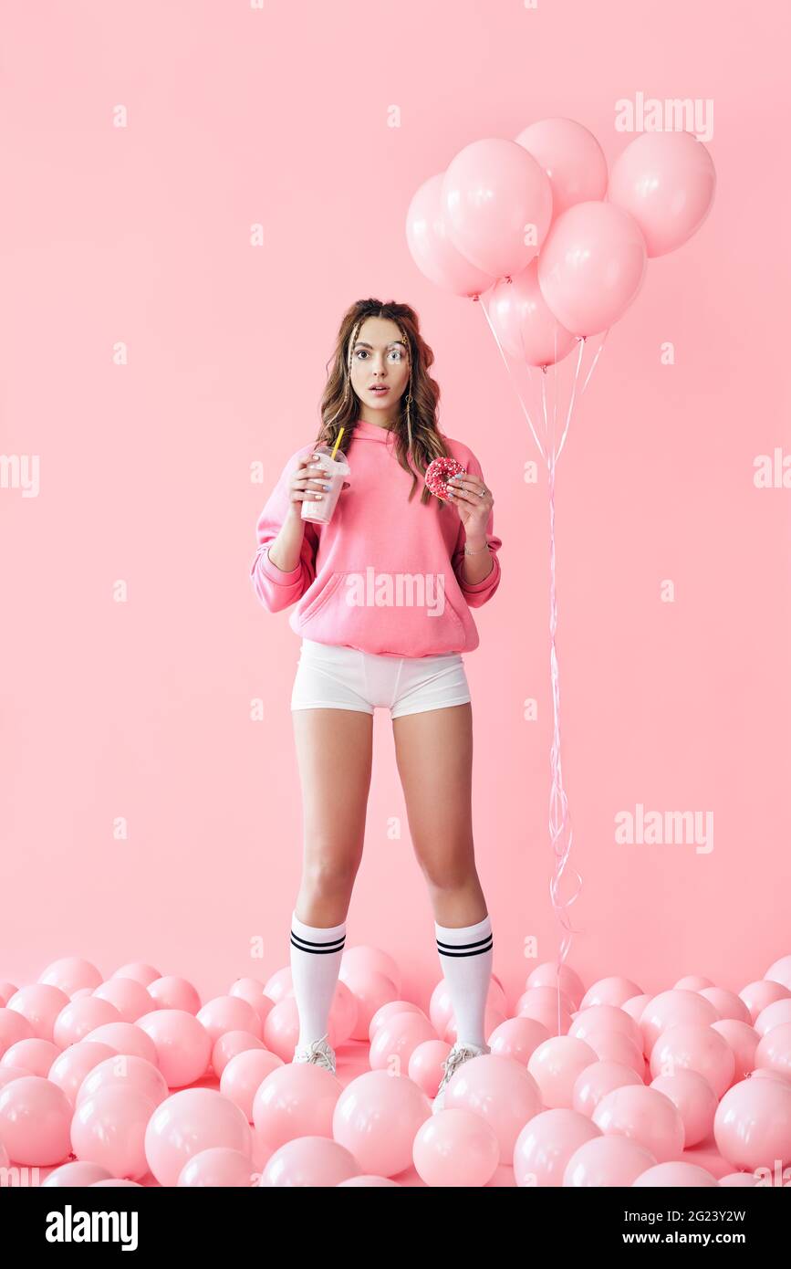Funny amazed woman with milkshake and donut in hands standing over air ...