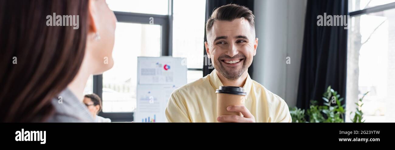 Positive businessman with coffee to go looking at blurred colleague ...