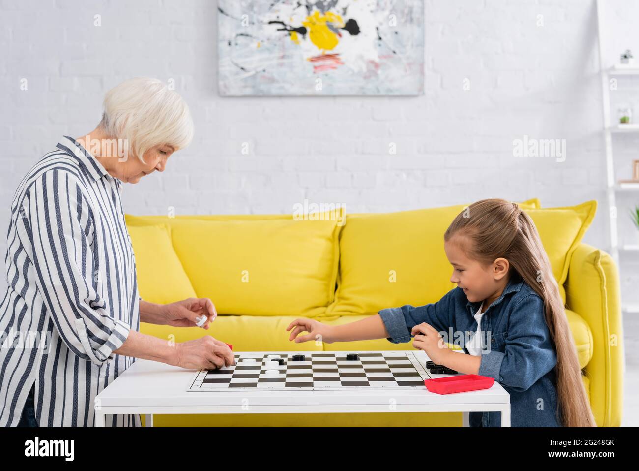 Side view of elderly woman playing checkers with granddaughter in ...