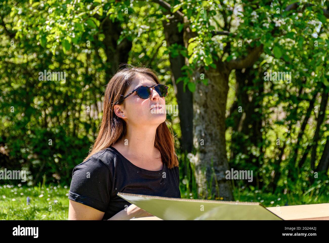 Beautiful young woman sitting outdoor in back yard unwrapping birthday ...