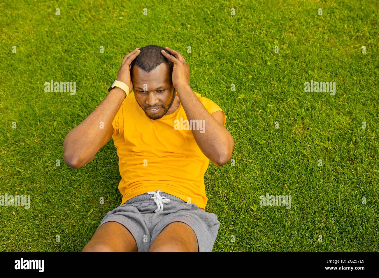 Young sporty focused Afro American male lying on green grass doing ...