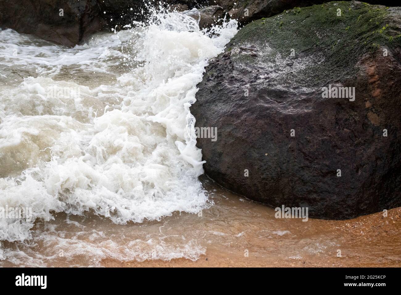 Close-up shot of the foamy waves of the ocean hitting mossy rock Stock ...
