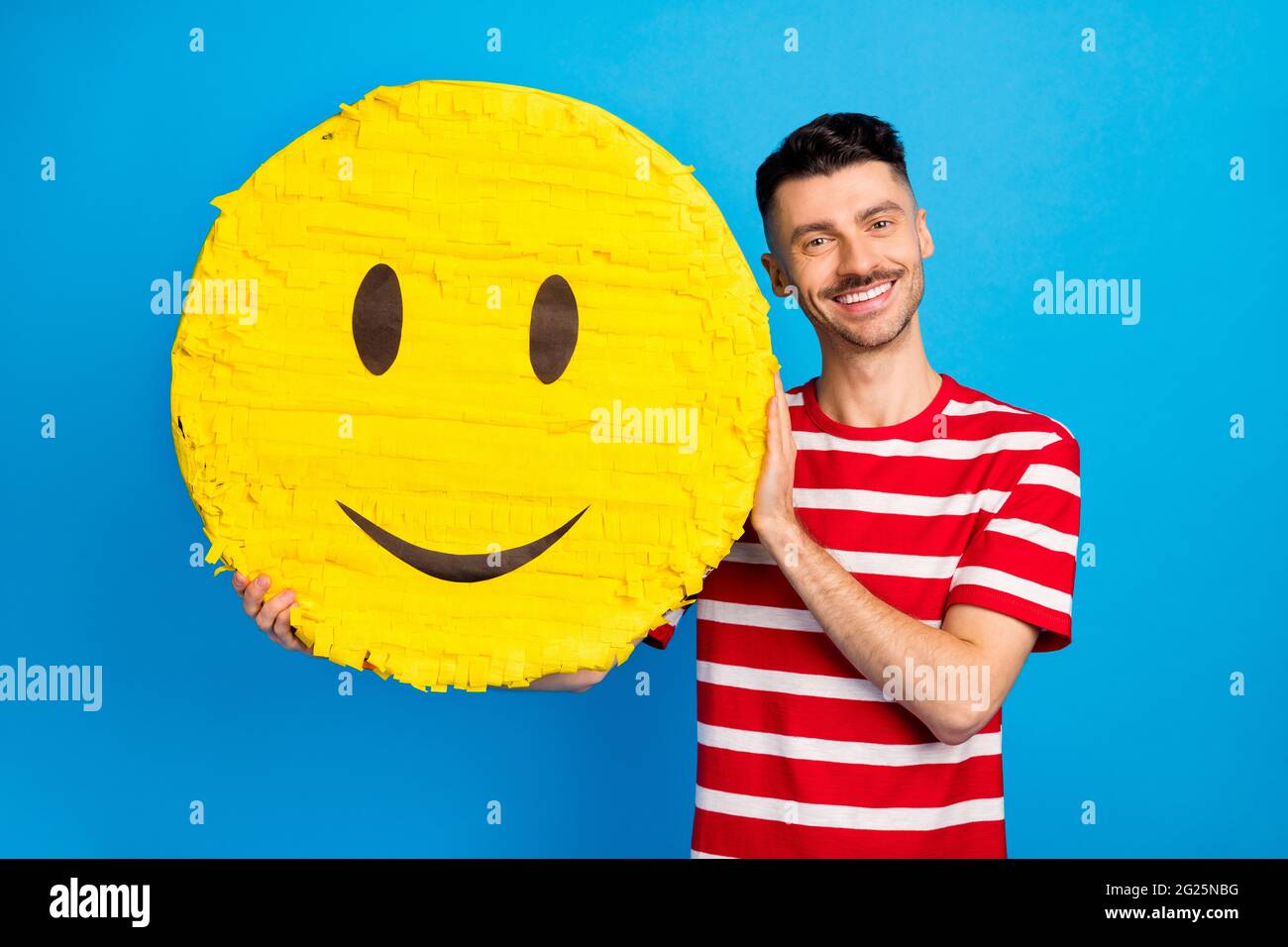 Photo of cheerful young happy man hold big face pinata smile emoji ...