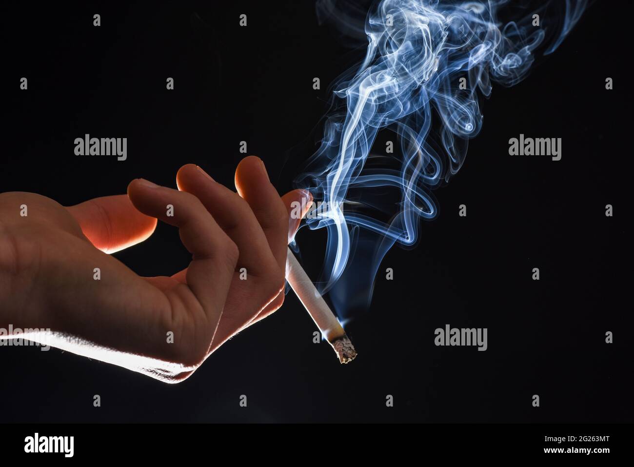 Male hand hold smoking cigarette with smoke stream dark background, bad ...