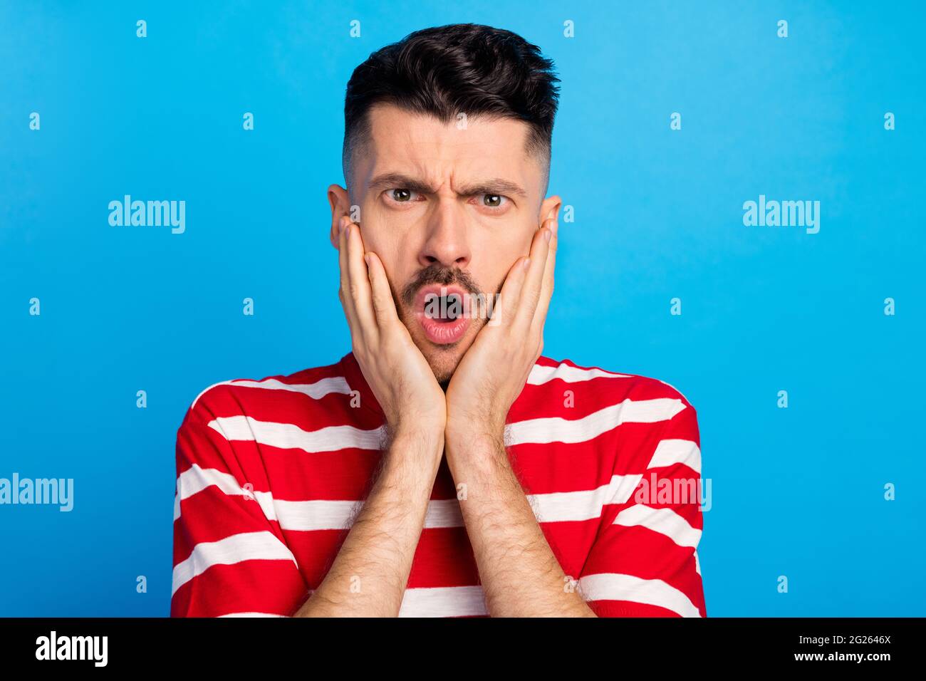 Photo of shocked impressed young man wear striped t-shirt arms cheeks ...