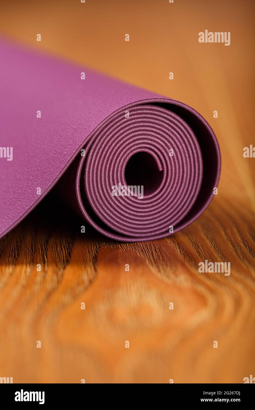A lilac-colored yoga mat is spread out in a roll on the wooden floor ...