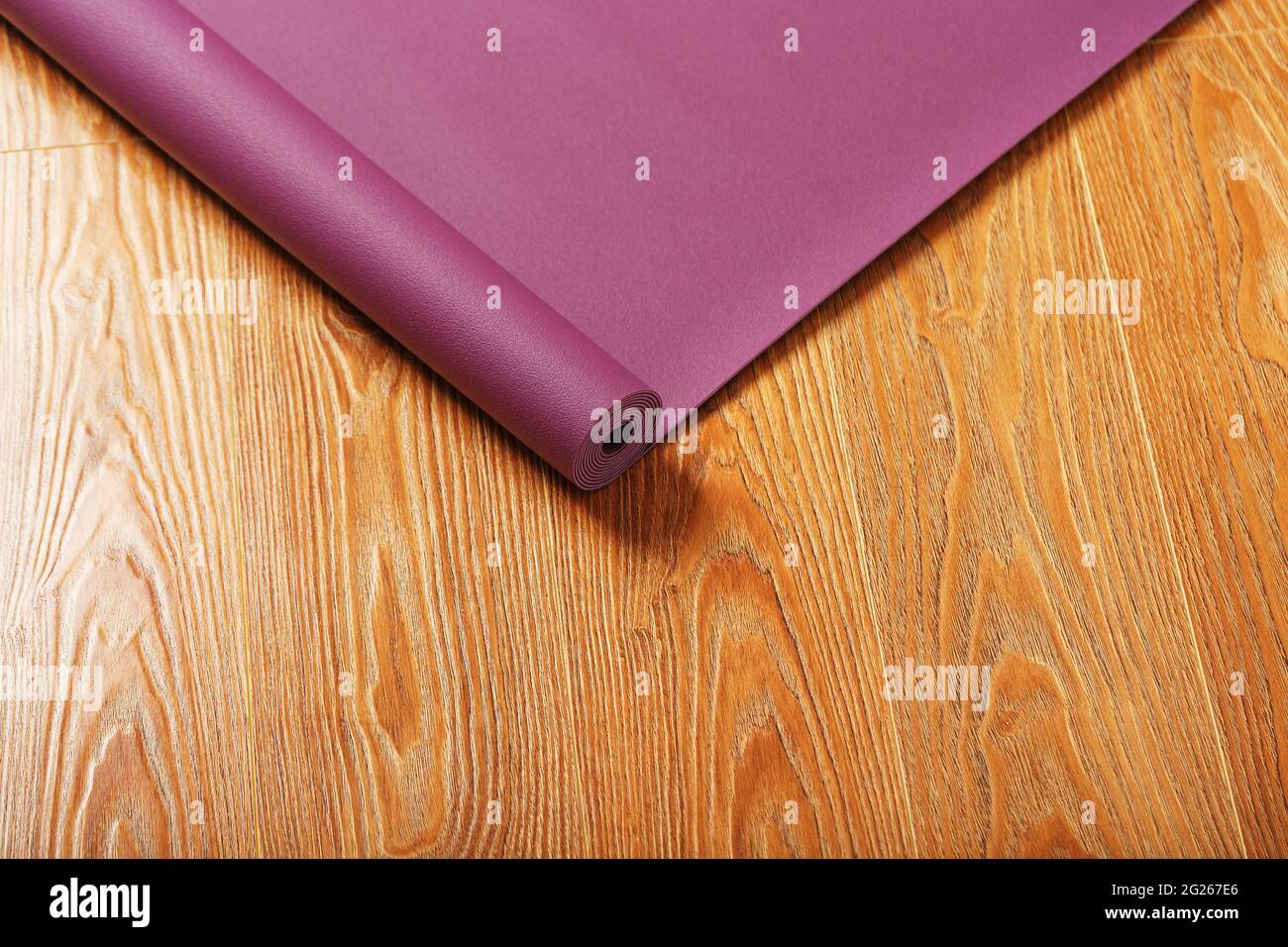 An unfolded lilac-colored yoga mat is unfolded on the wooden floor. Top ...