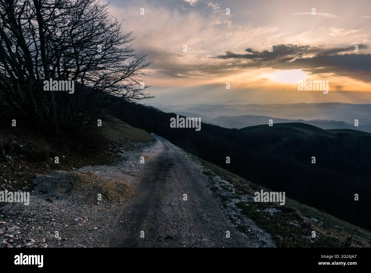 A mountain path with distant sunset, mist and sunrays between valley ...
