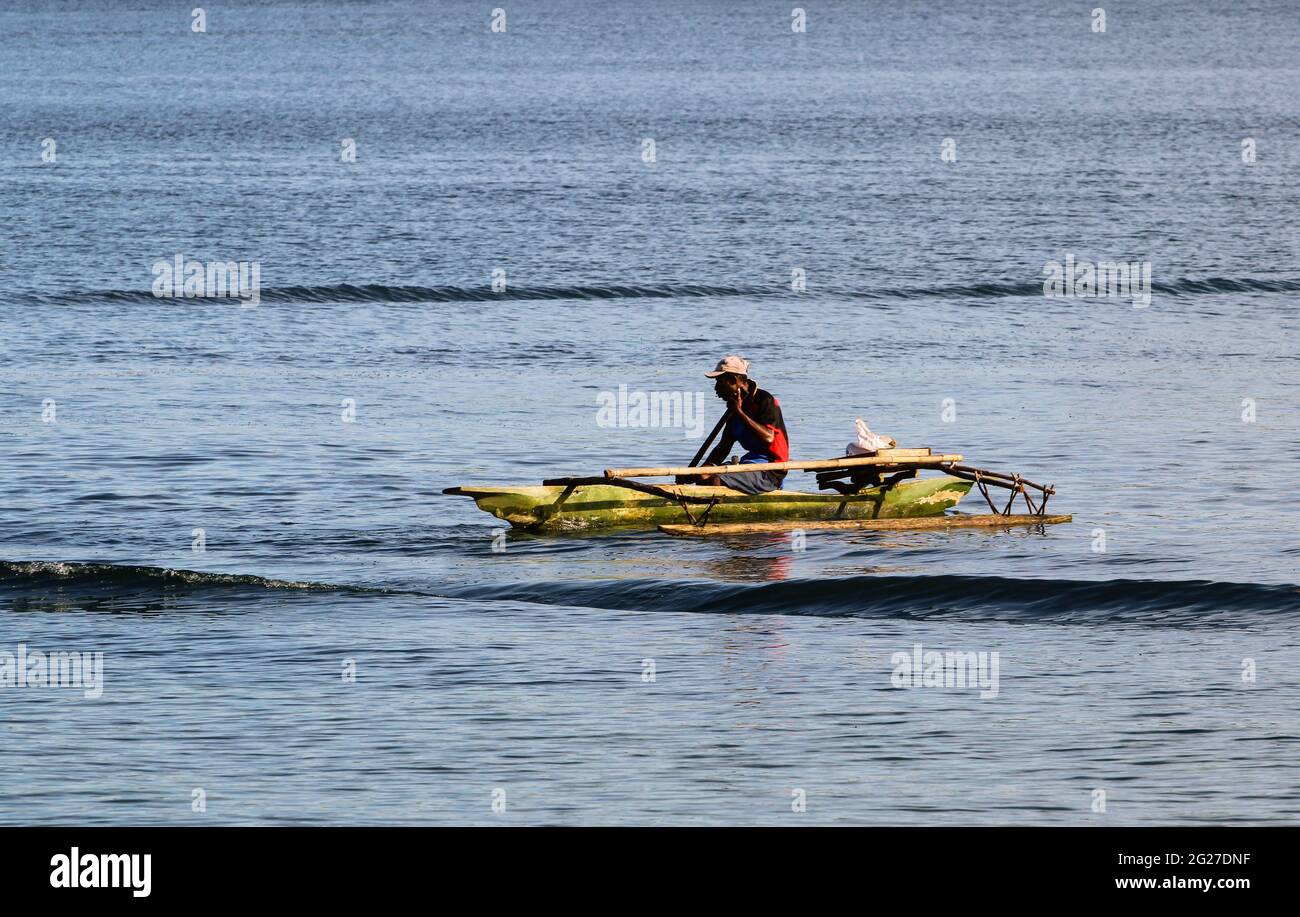 A lone paddler in a dugout outrigger canoe in the waters outside of ...