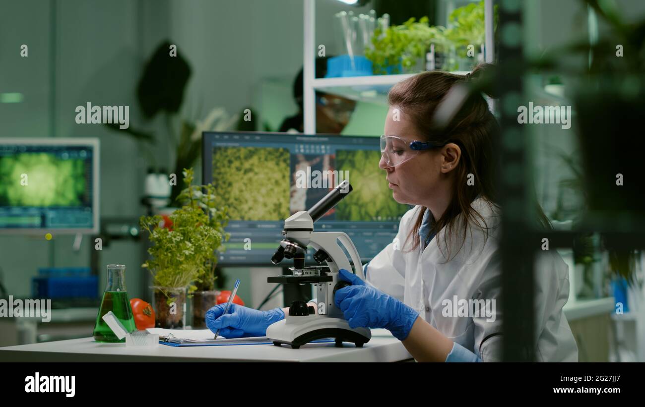 Pharmaceutical scientist looking at green leaf sample on microscope ...