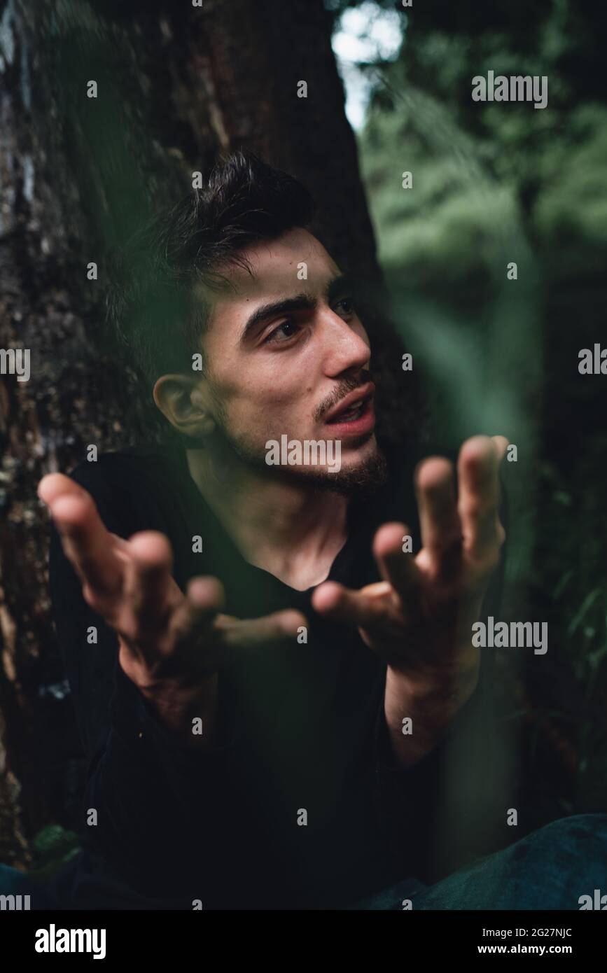 The young man leaning on a tree in the forest asks why, nature and ...